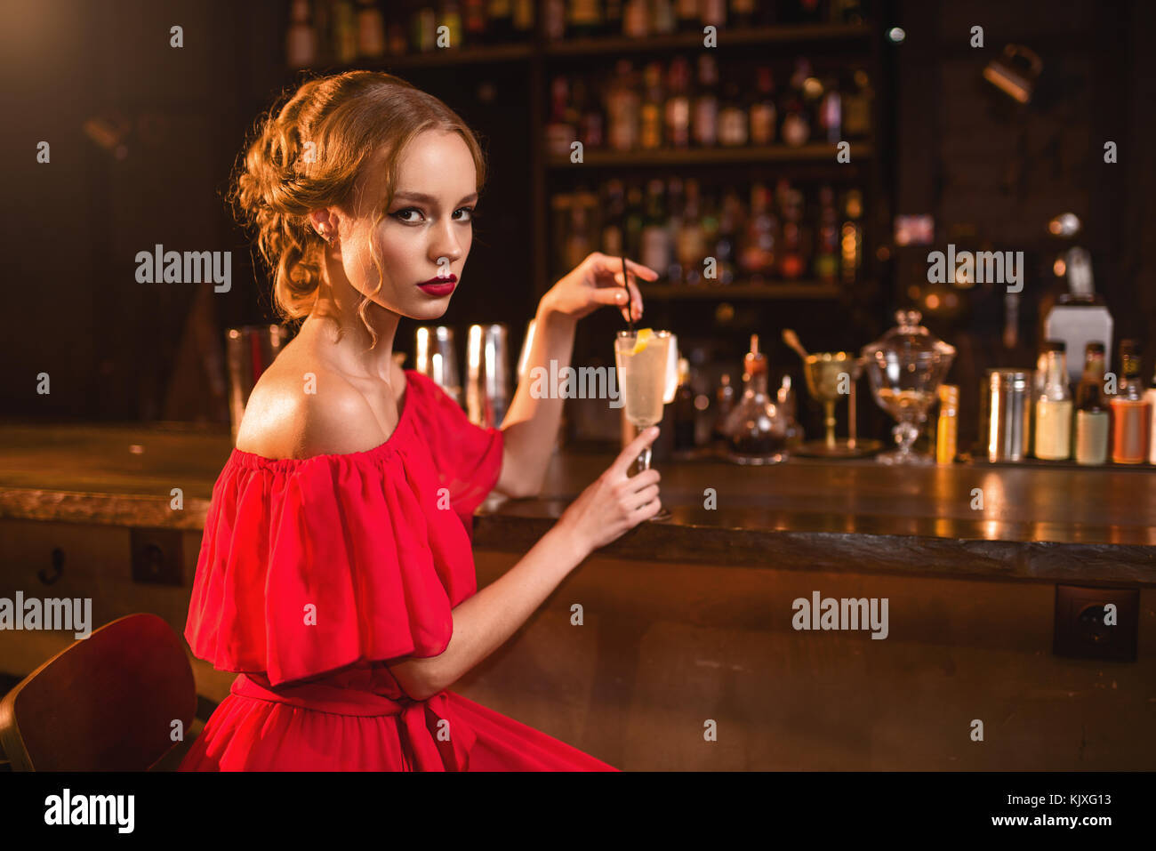 Beautiful woman in red dress drinks alcohol cocktail at the bar counter ...