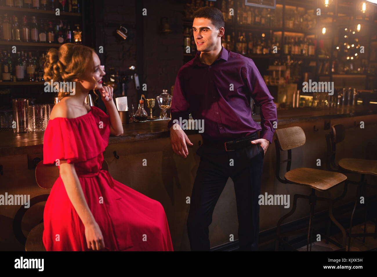 Acquaintance in bar, beautiful woman in red dress flirts with man ...