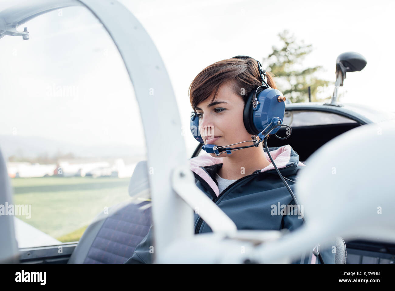Smiling female pilot in the light aircraft cockpit, she is wearing ...