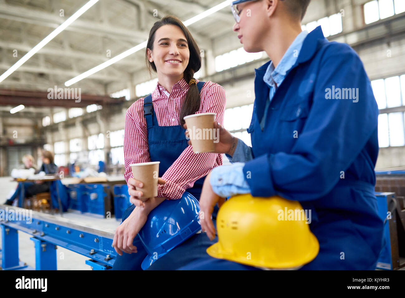 Positive young female construction workers drinking coffee from ...