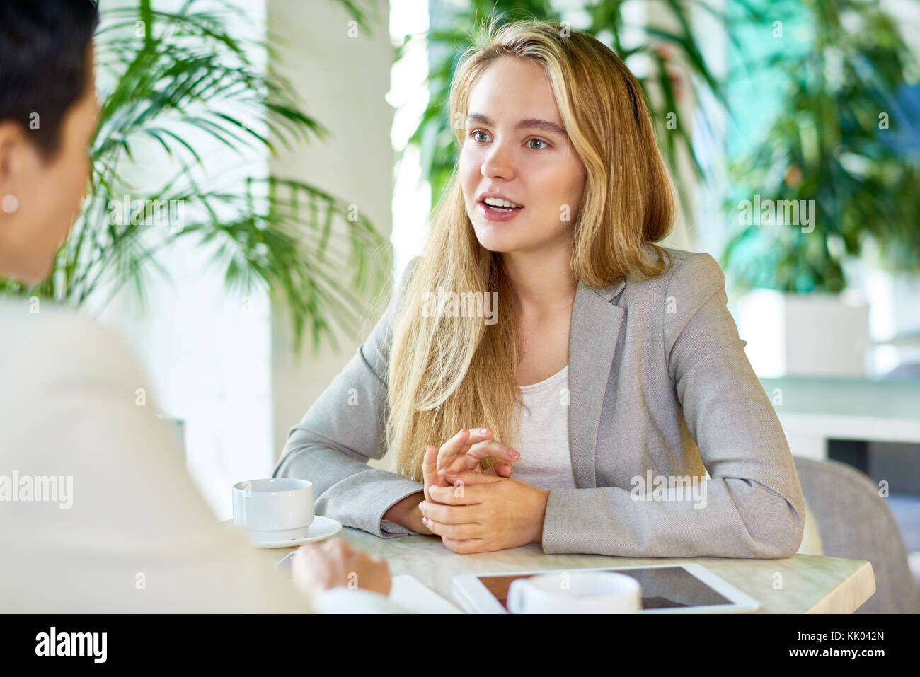 Portrait of two modern young women discussing work sitting at table in ...