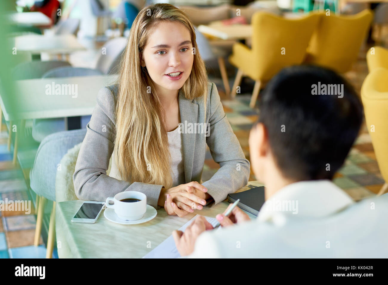 Portrait of two modern young women discussing work sitting at table in ...