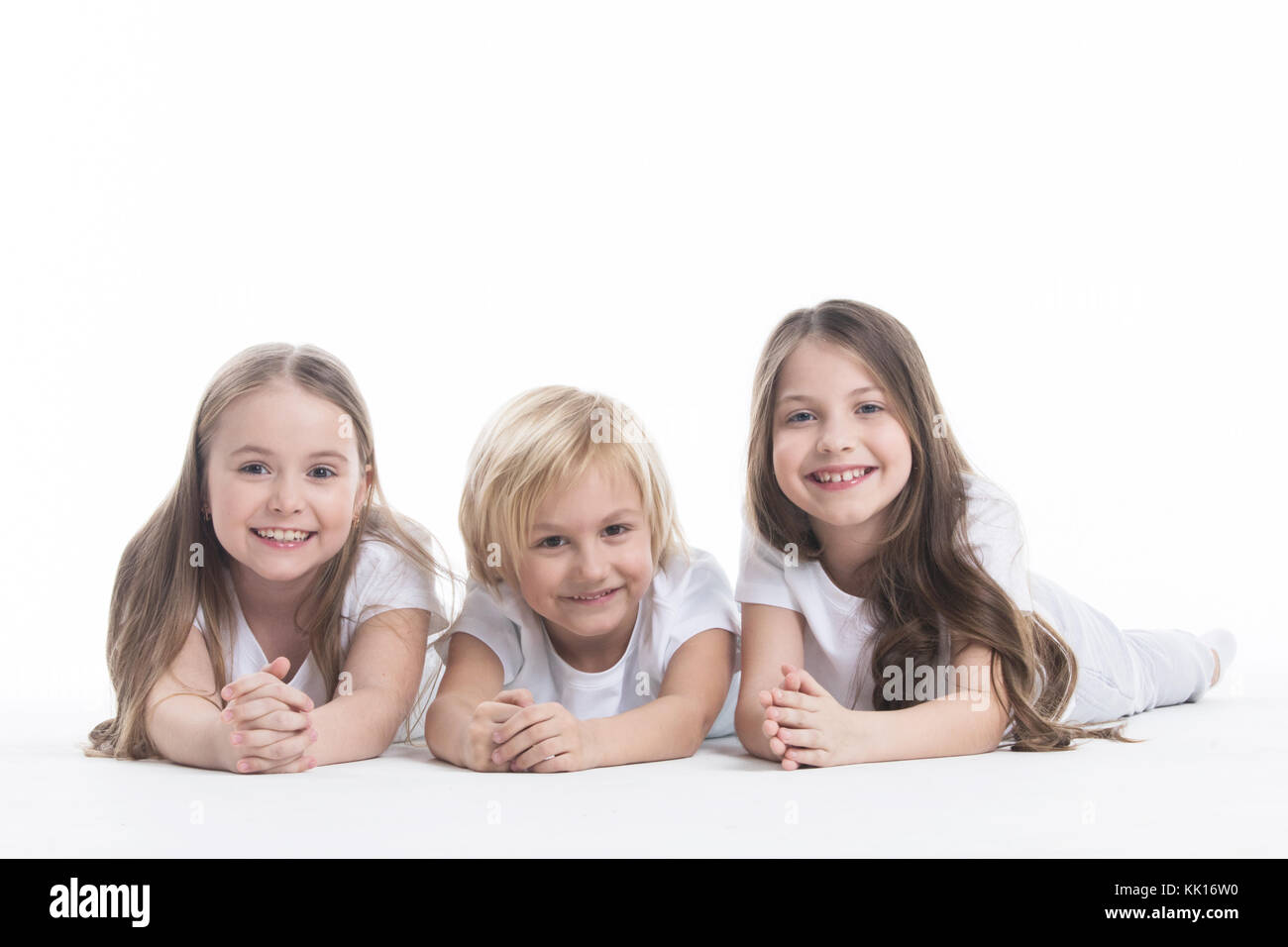 Happy smiling three children in white clothes laying on floor isolated ...