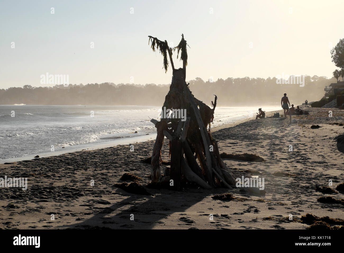 A driftwood sculpture and couples sitting on the sand at sunset at ...