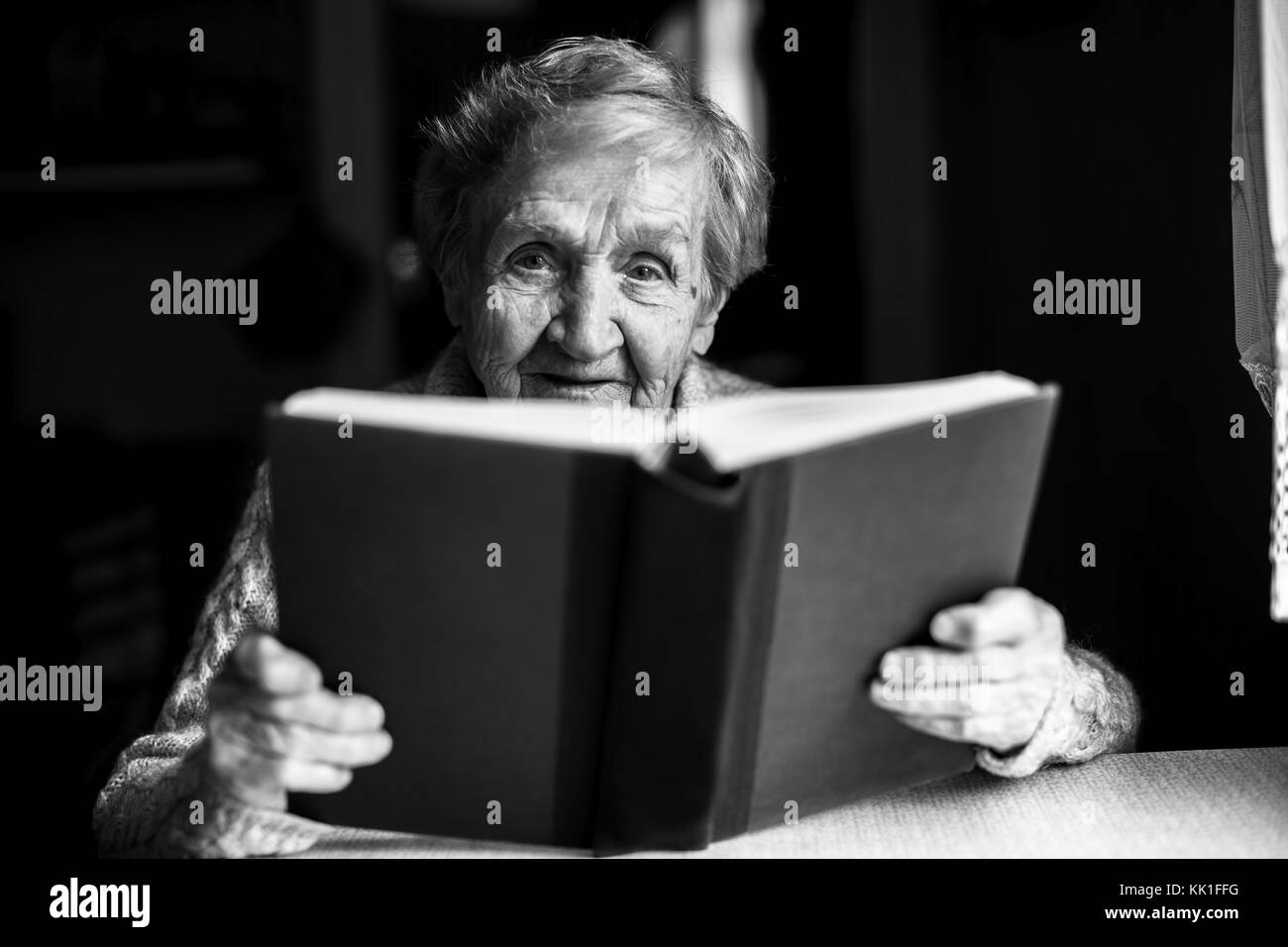 An elderly woman reads the book sitting at the table. Black and white ...