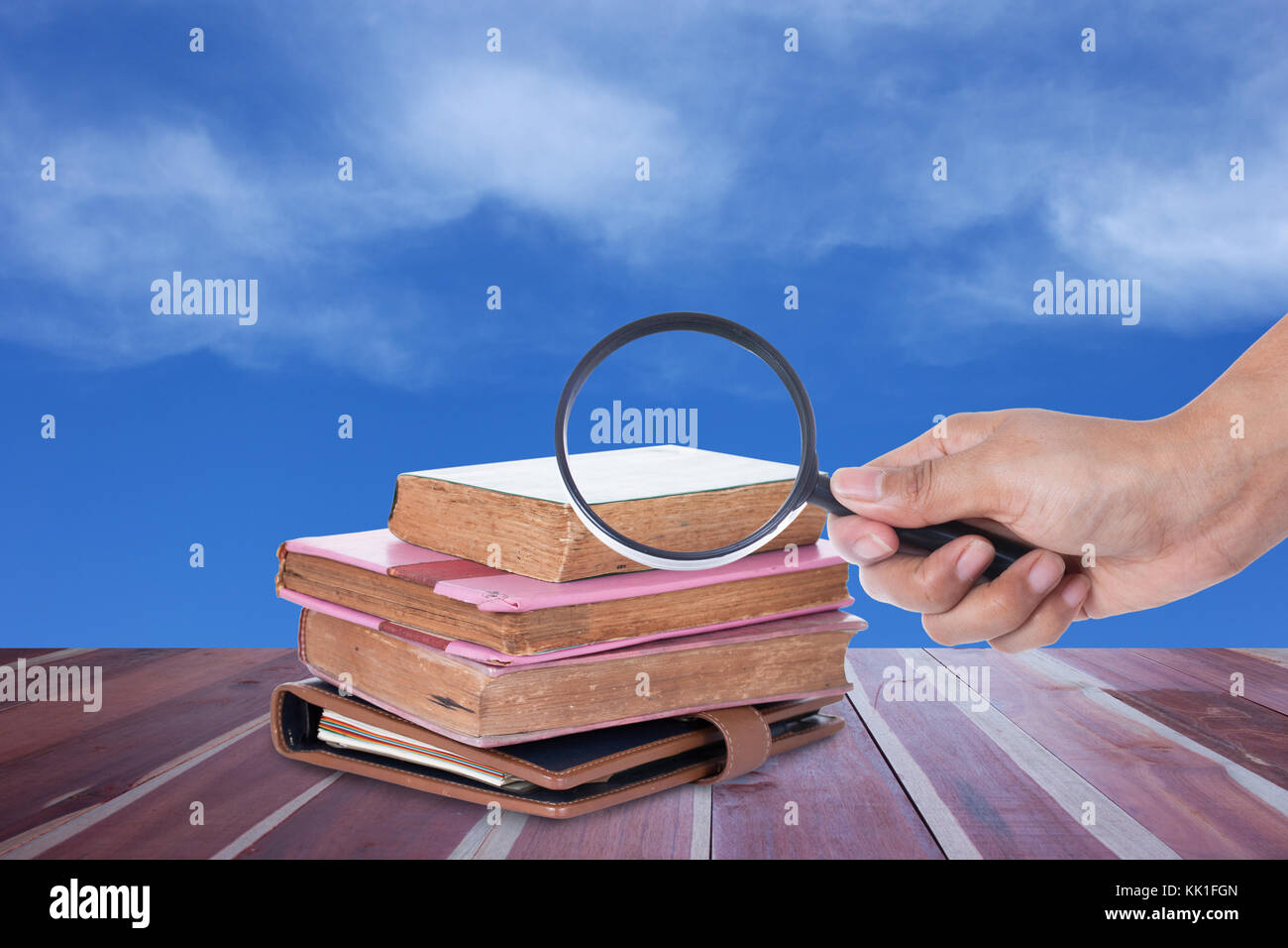 Hand holding magnifying glass over book with blue sky Stock Photo - Alamy