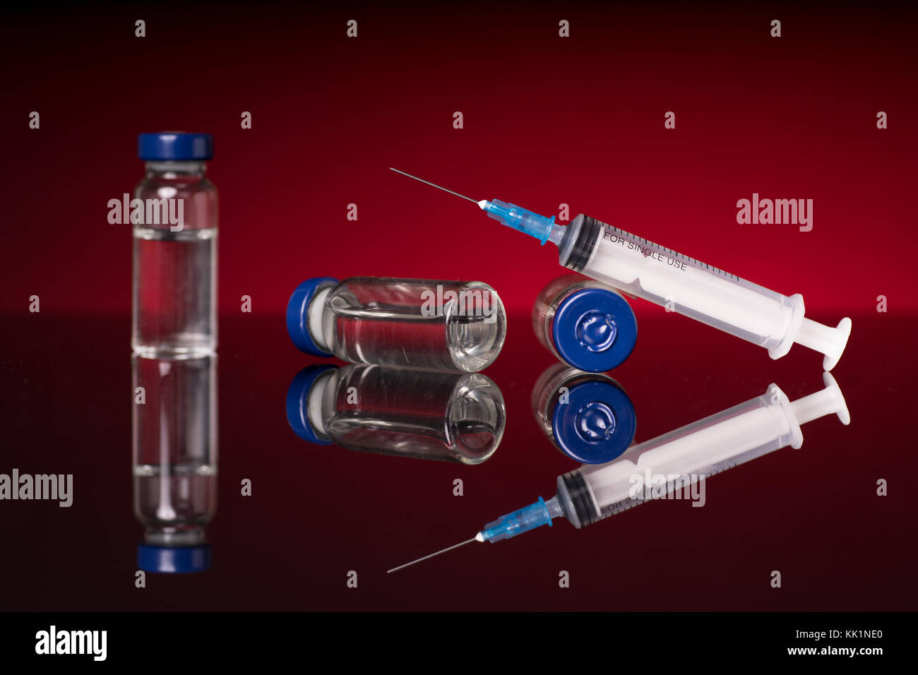 Syringe and medical vials isolated on red dark background with glossy ...