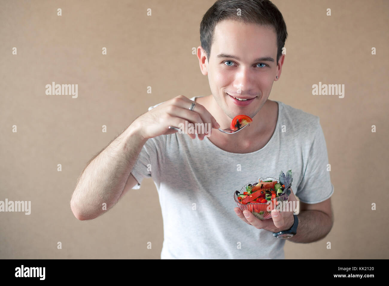 Slim handsome boy eating salad over wooden background. studio shot ...