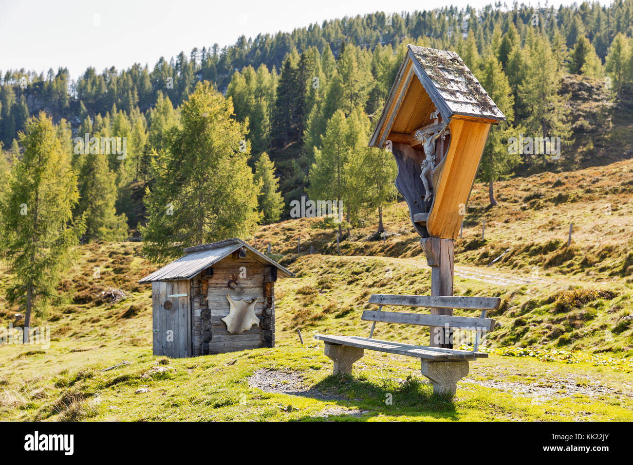 Old wooden crucifix, bench and toilet on a highland pasture with Alpine ...