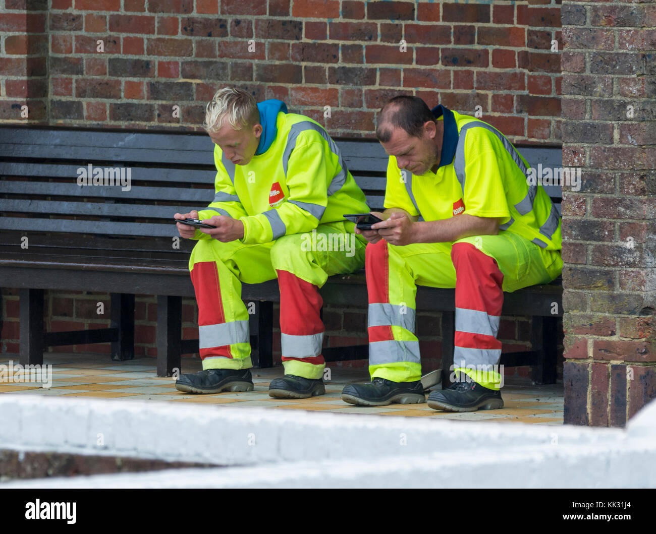 Pair of male workmen sitting taking a break while using mobile phones ...