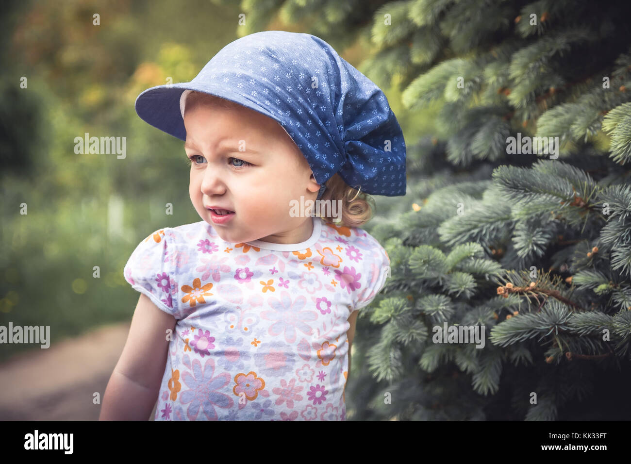 Mischievous frouned child girl portrait among fir trees on blurred ...