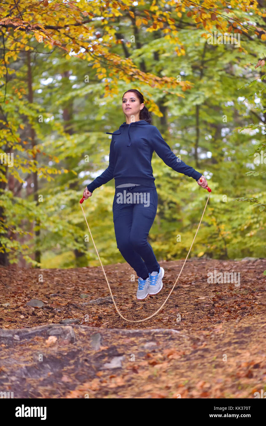 Sporty young woman jumping rope in park with autumn colors background ...