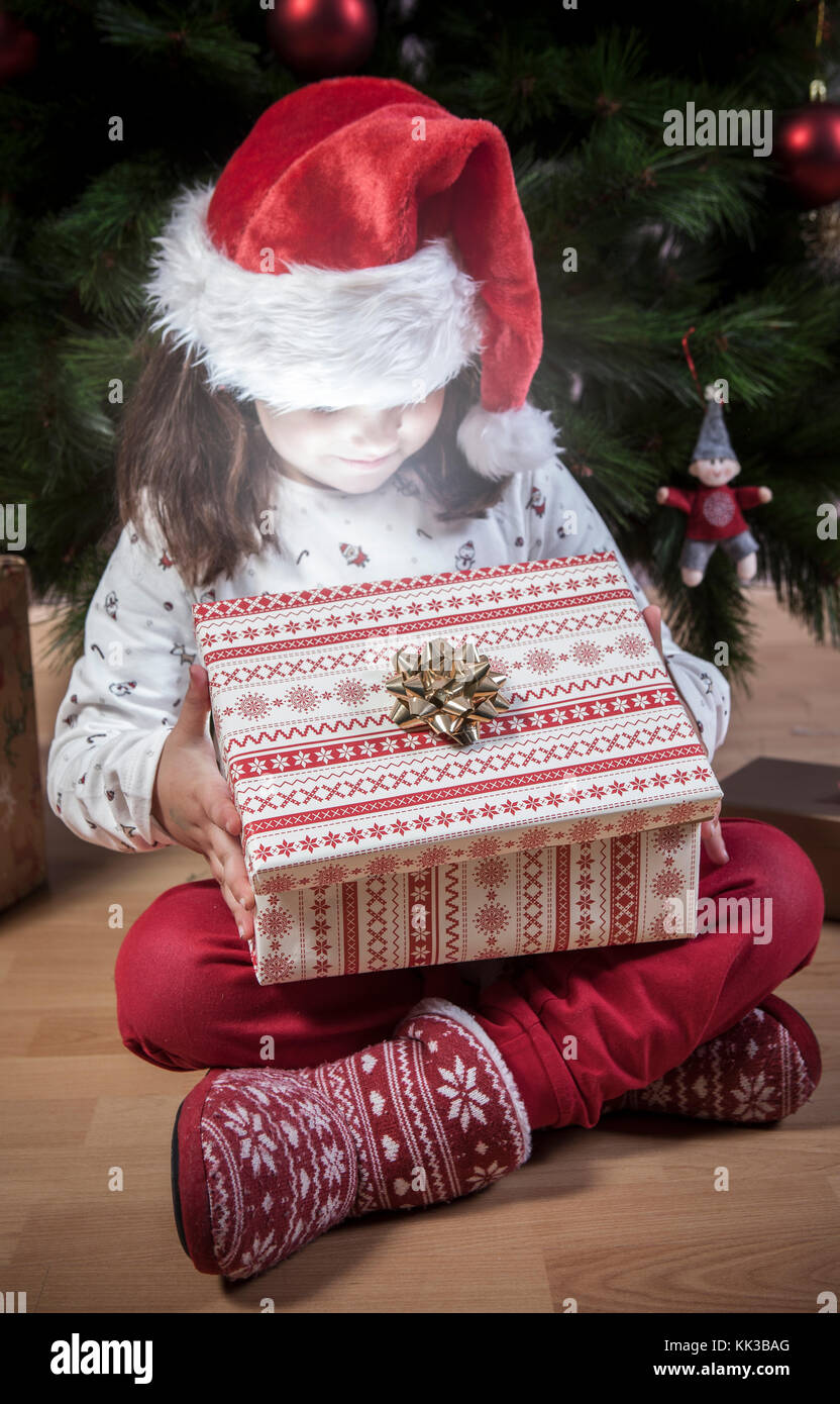 Little girl opening her present beside Christmas tree. She is ...