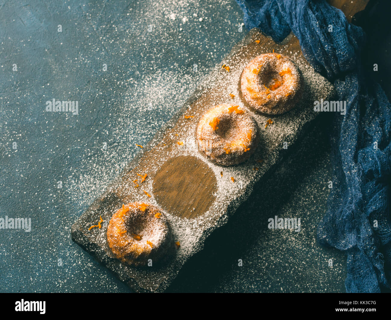 Mini bundt ring cakes with orange zest icing sugar on dark blue ...