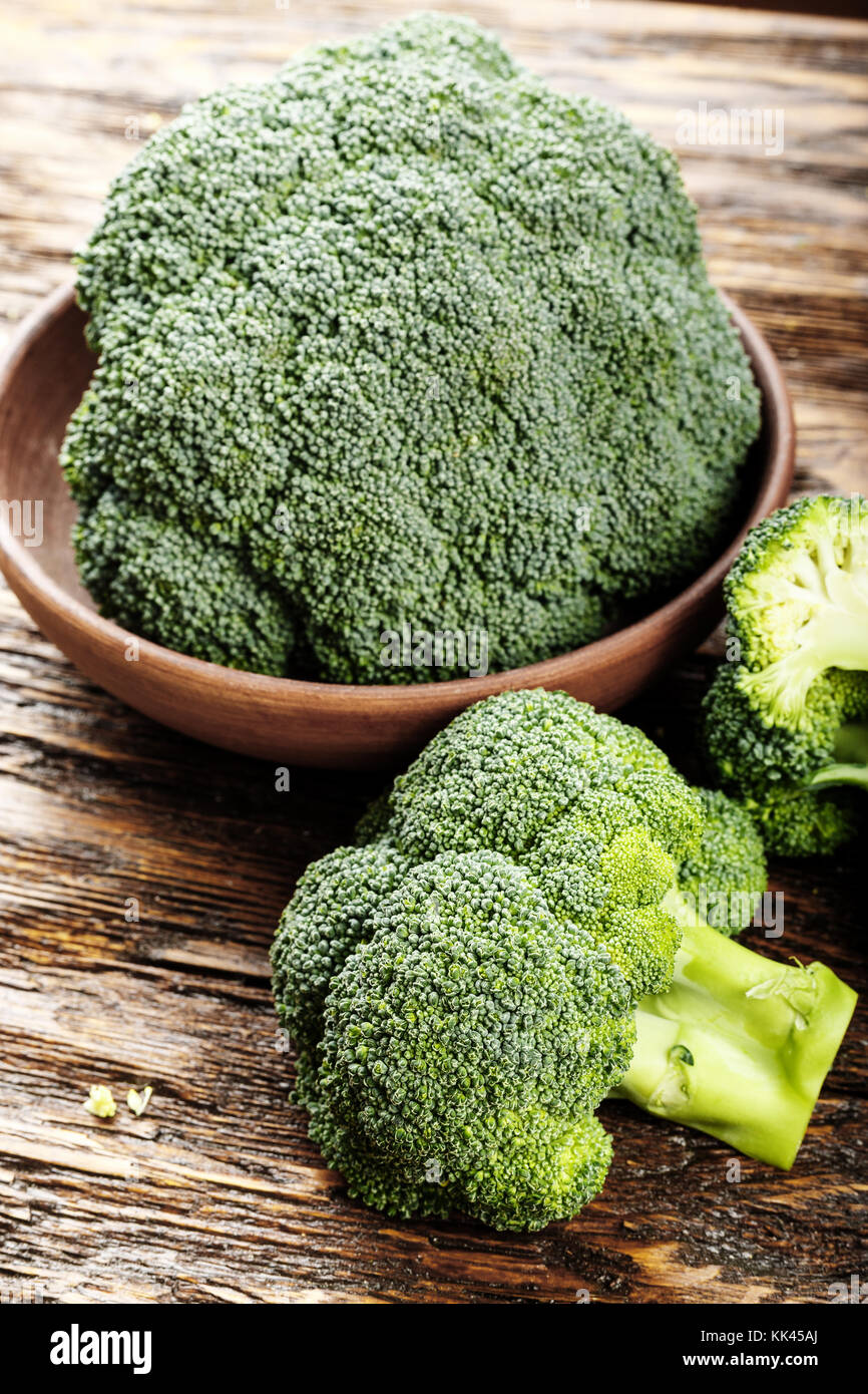 broccoli in a clay plate on a wooden table, next to a whole cabbage are ...