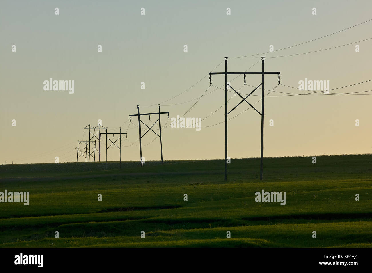 Rural scene with silhouette of electricity pylons on a green hill ...