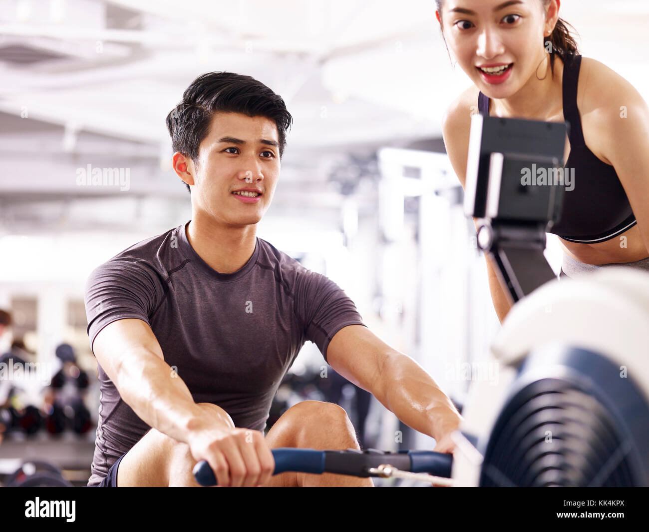 young asian man and woman working out in fitness center using rowing ...
