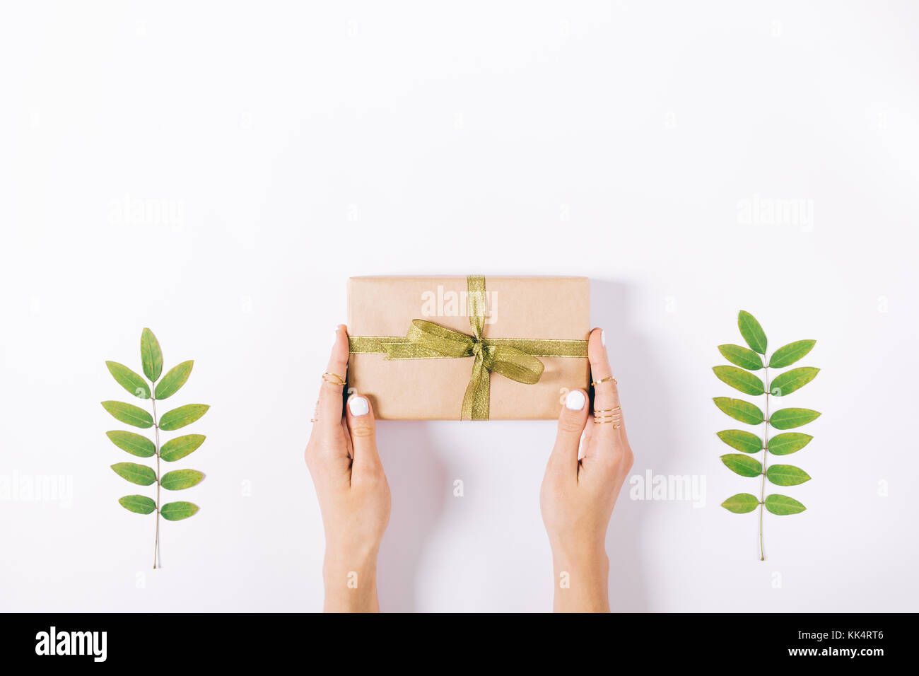 Female hands holding a box with a gift and ribbon on a white table top ...