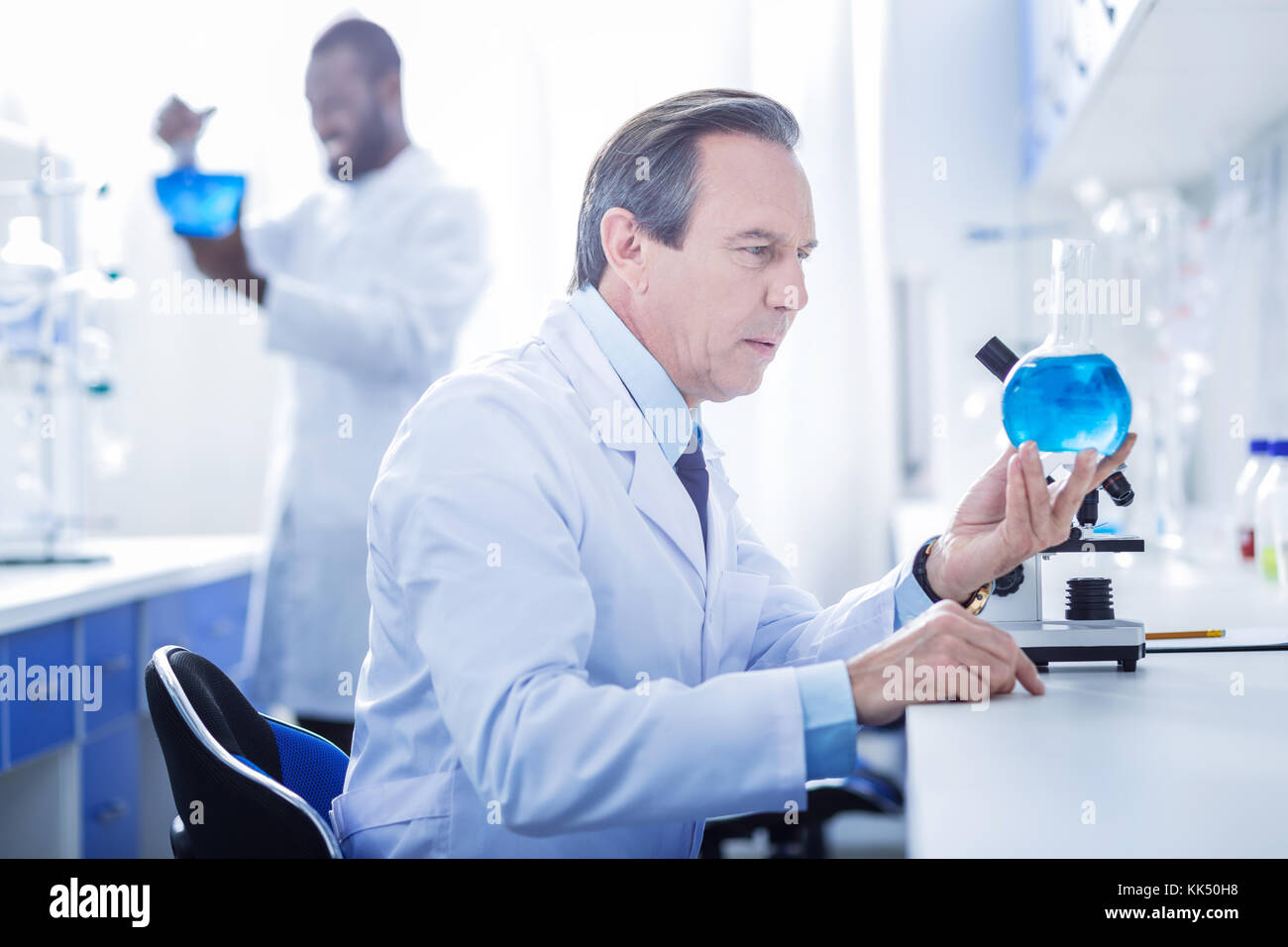 Serious smart scientist looking at the blue liquid Stock Photo - Alamy
