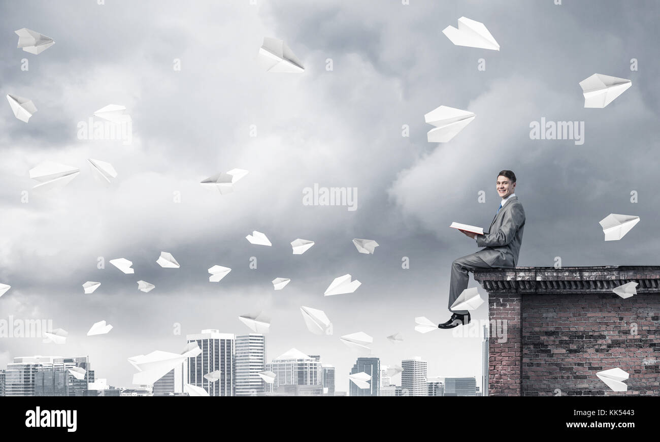 Man on roof edge reading book and cityscape at background Stock Photo ...