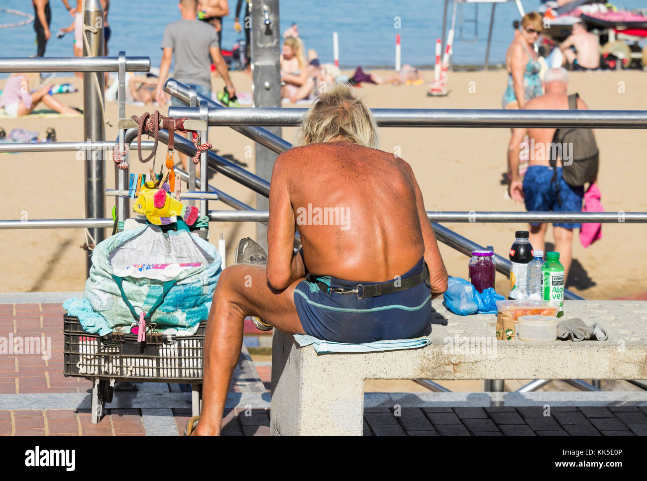 Homeless man eating on bench overlooking tourist beach in Spain Stock ...