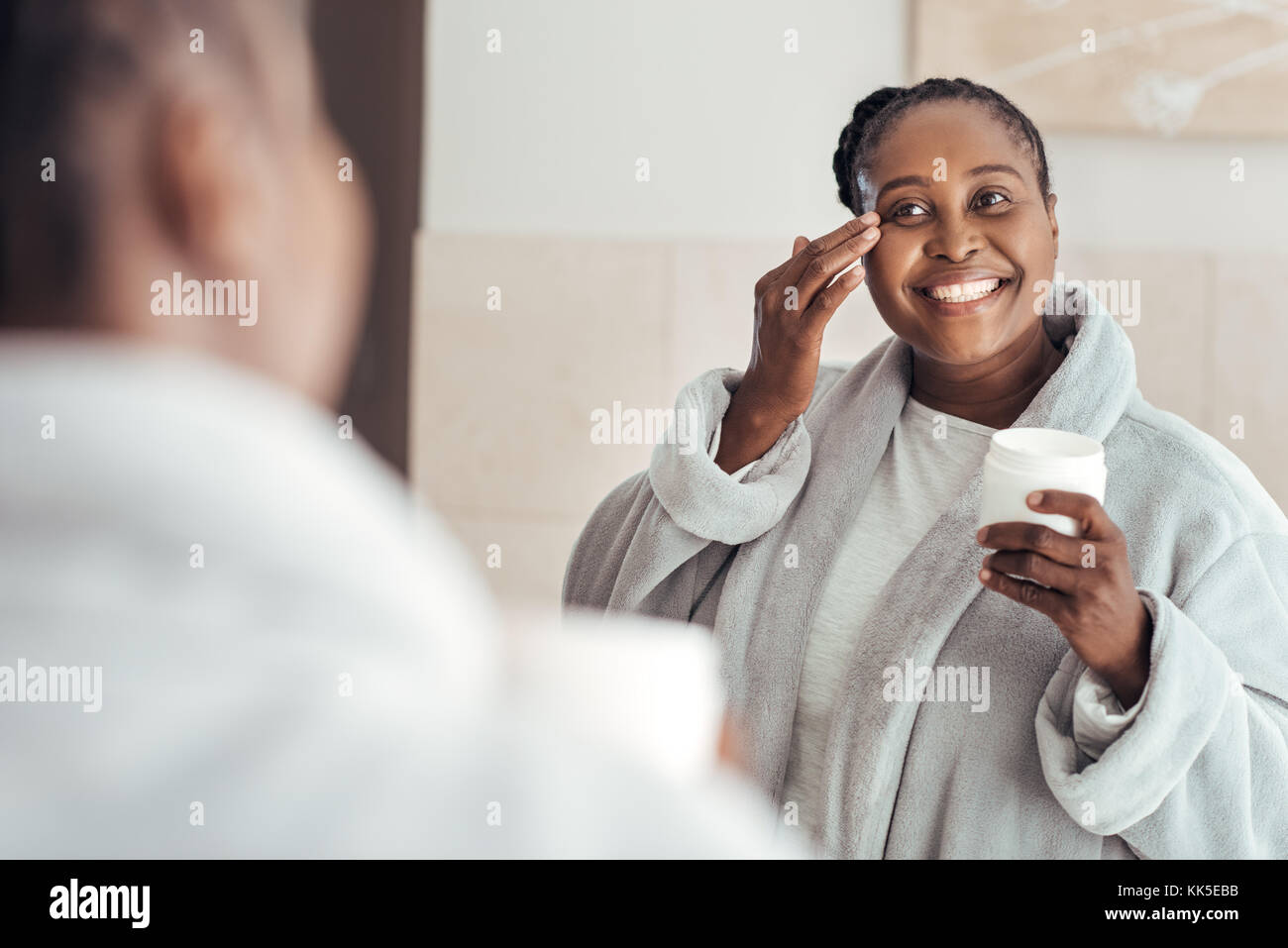 Smiling young African woman putting on face cream at home Stock Photo ...