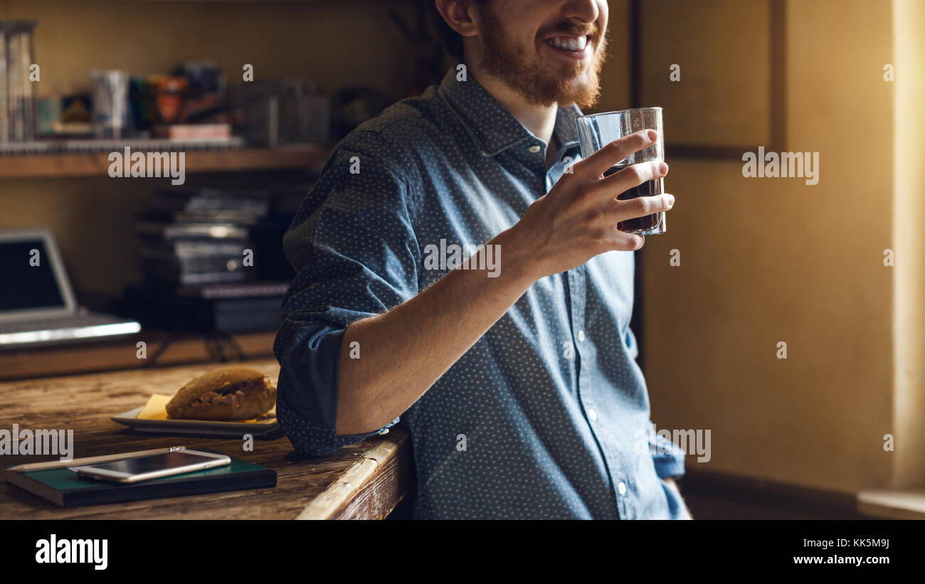 Hipster young smiling man drinking a glass of coke and leaning on a ...