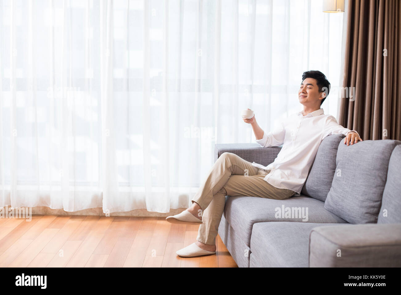 Cheerful young Chinese man drinking coffee at home Stock Photo - Alamy