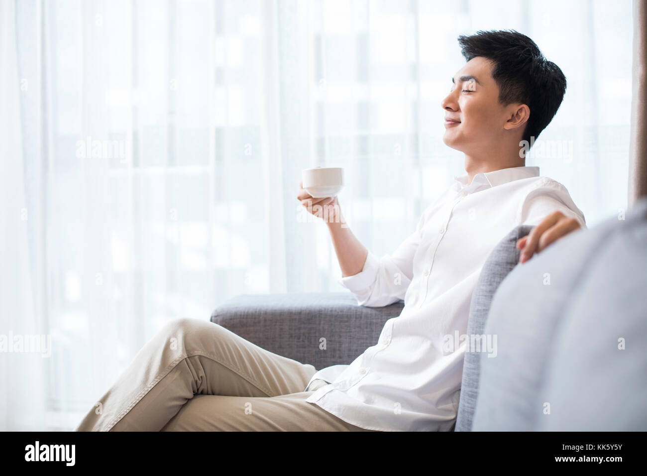 Cheerful young Chinese man drinking coffee at home Stock Photo - Alamy