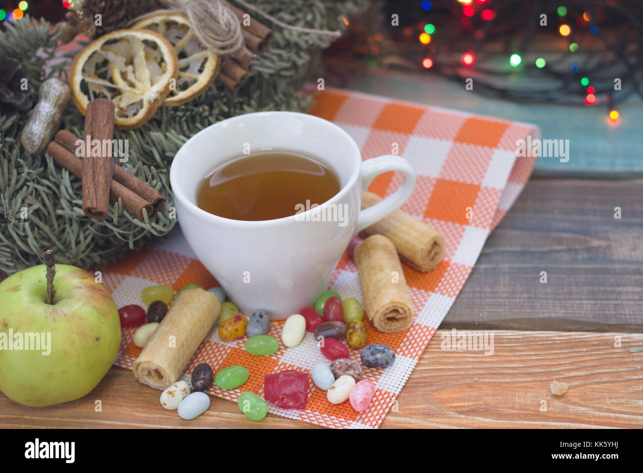 A festive still life with a cup of tea, an apple, candies and a wreath ...