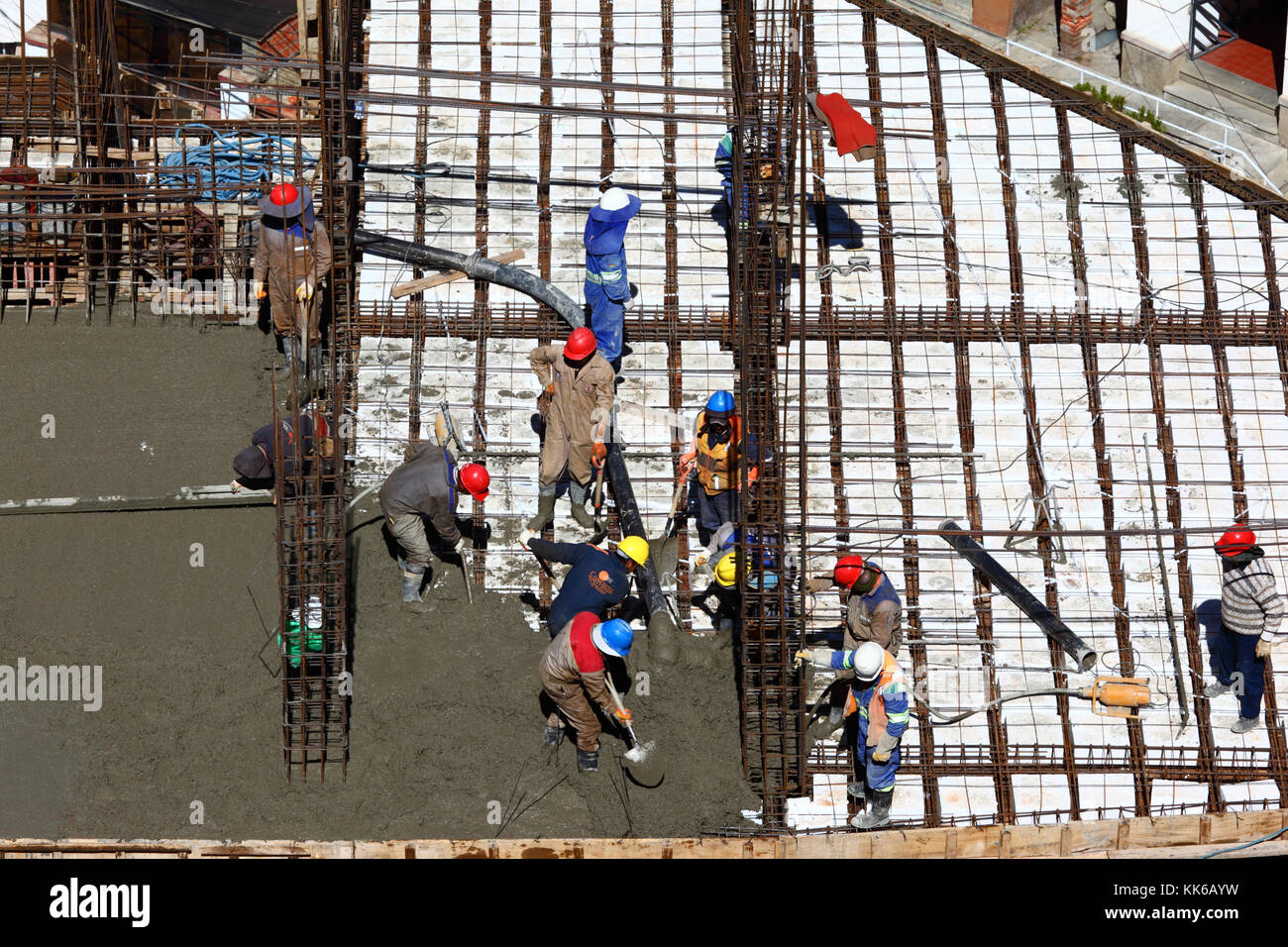 Workers on building site spreading wet concrete over polystyrene tiles ...