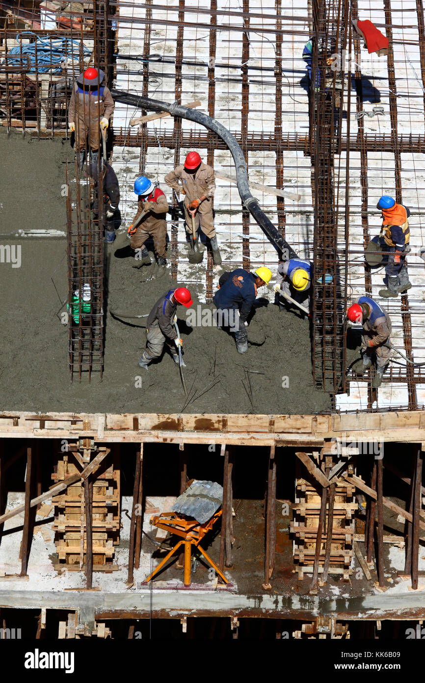 Workers on building site spreading wet concrete over polystyrene tiles ...