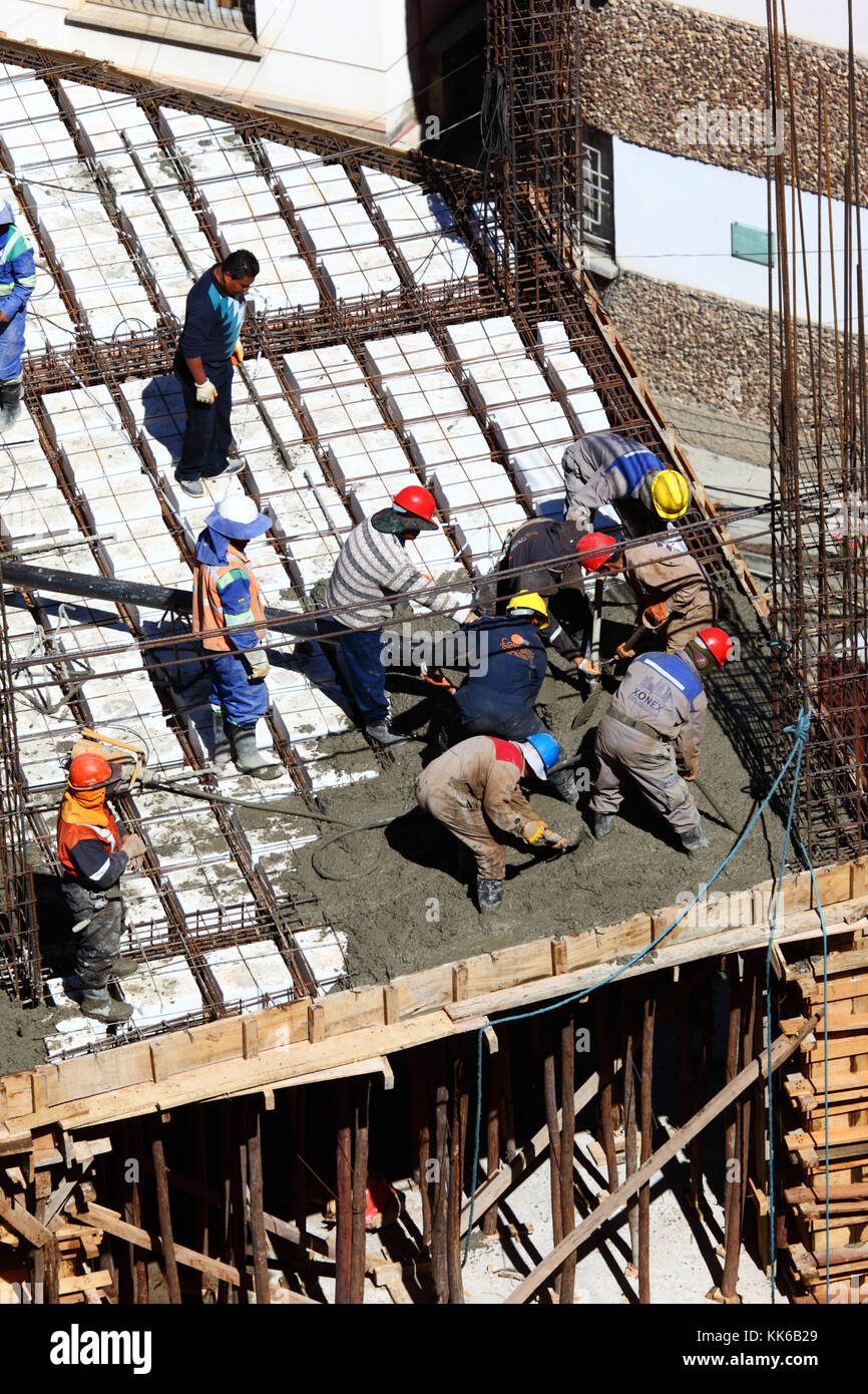 Workers on building site spreading wet concrete over polystyrene tiles ...
