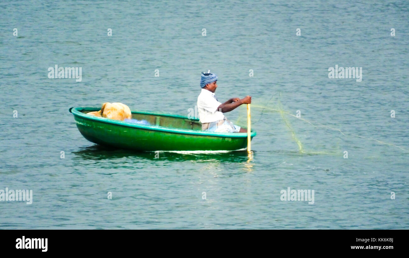 Man sailing a small round boat in the water reservoir throwing fish ...