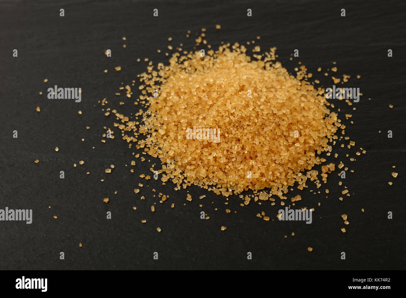 Close up pinch of brown cane sugar spilled on black slate board, high ...