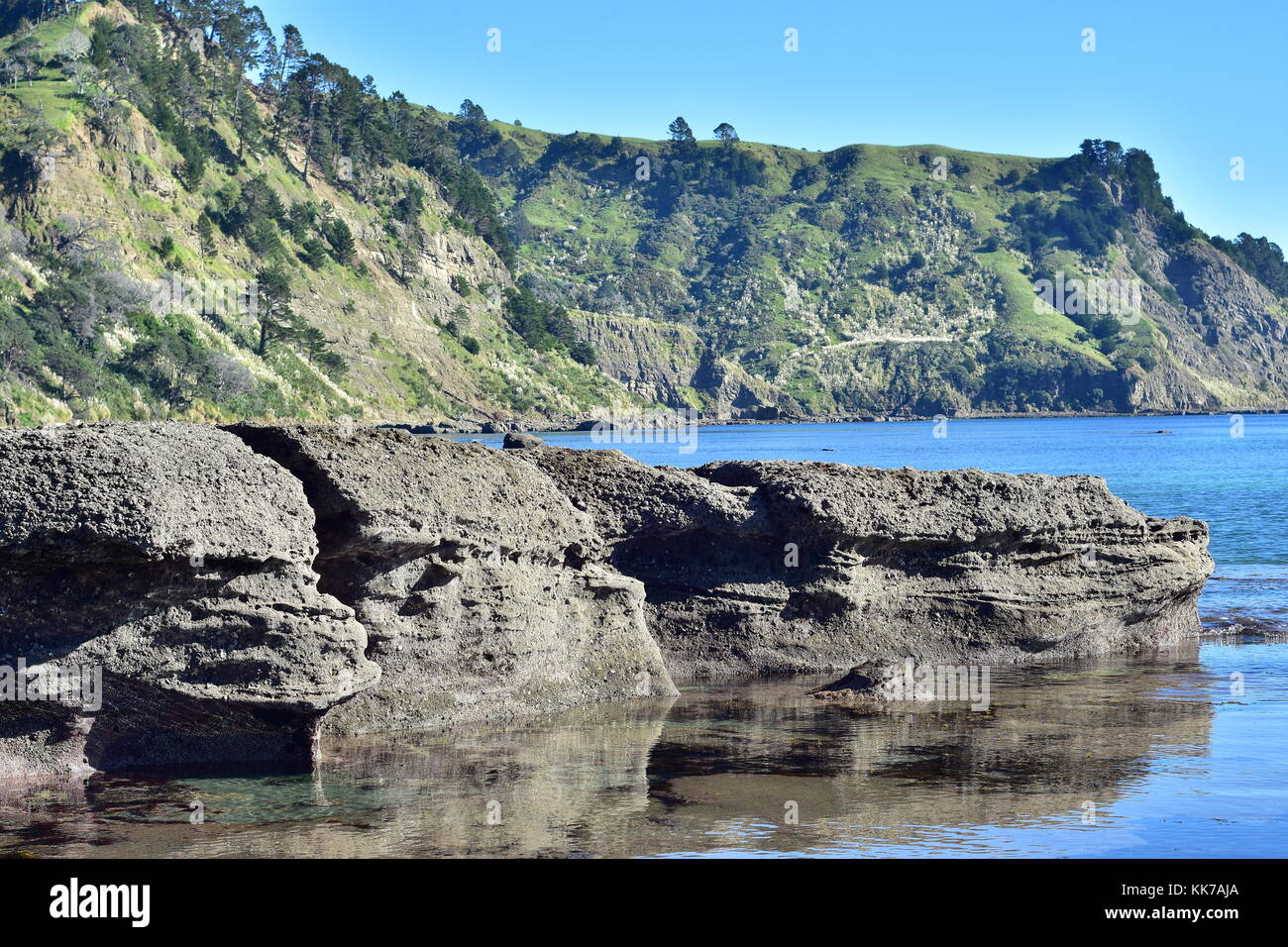 Coastal rocks emerging from calm sea with steep cliffs in background at ...
