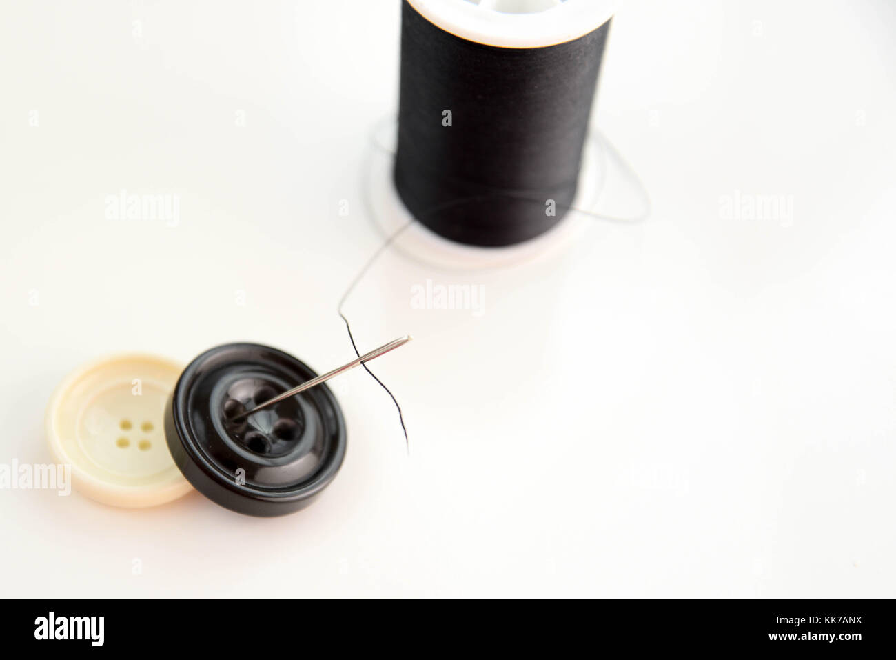 black spool of thread, threaded needle, and black and white buttons ...