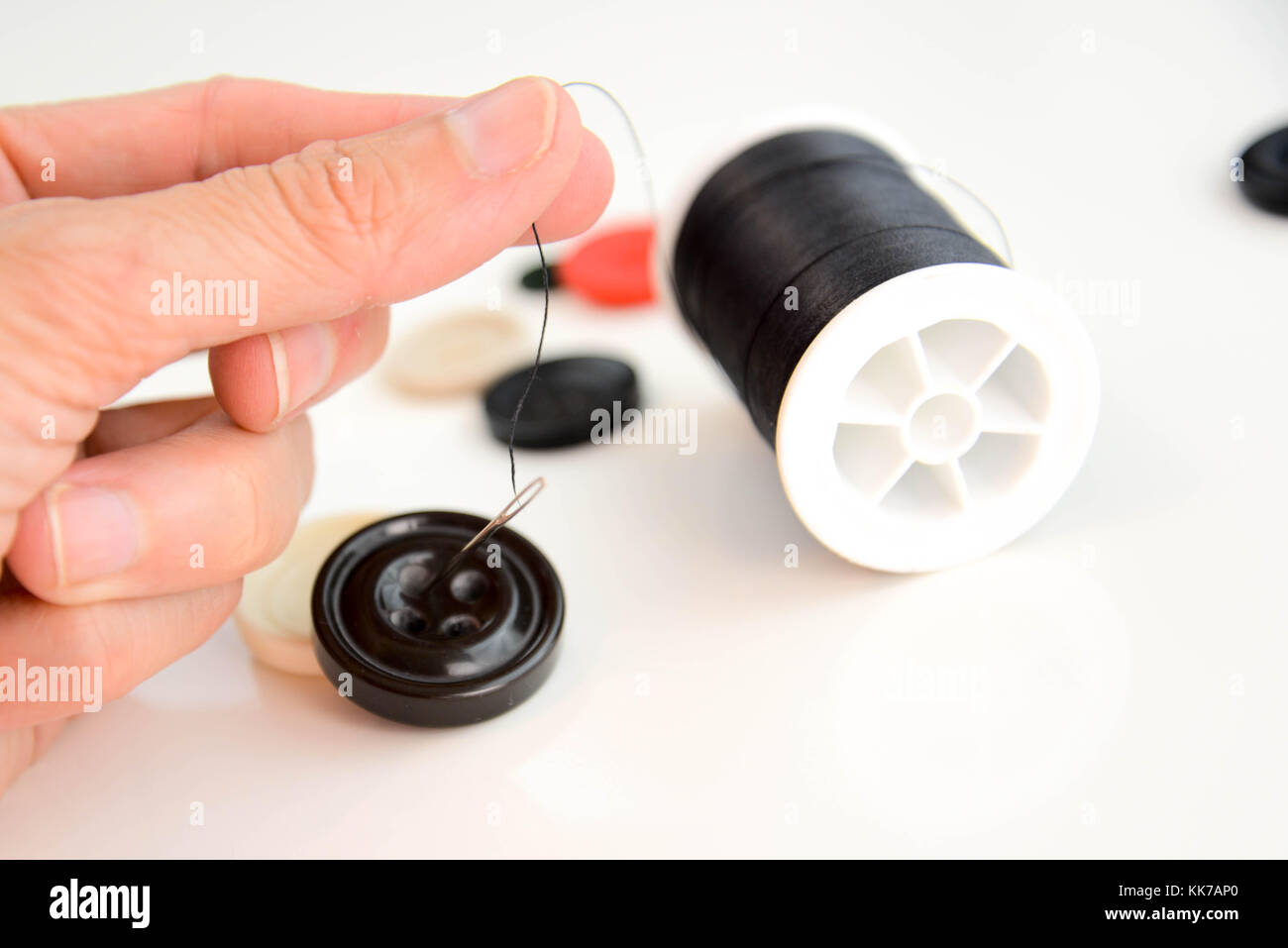 hand threading a needle with black thread. buttons Stock Photo - Alamy