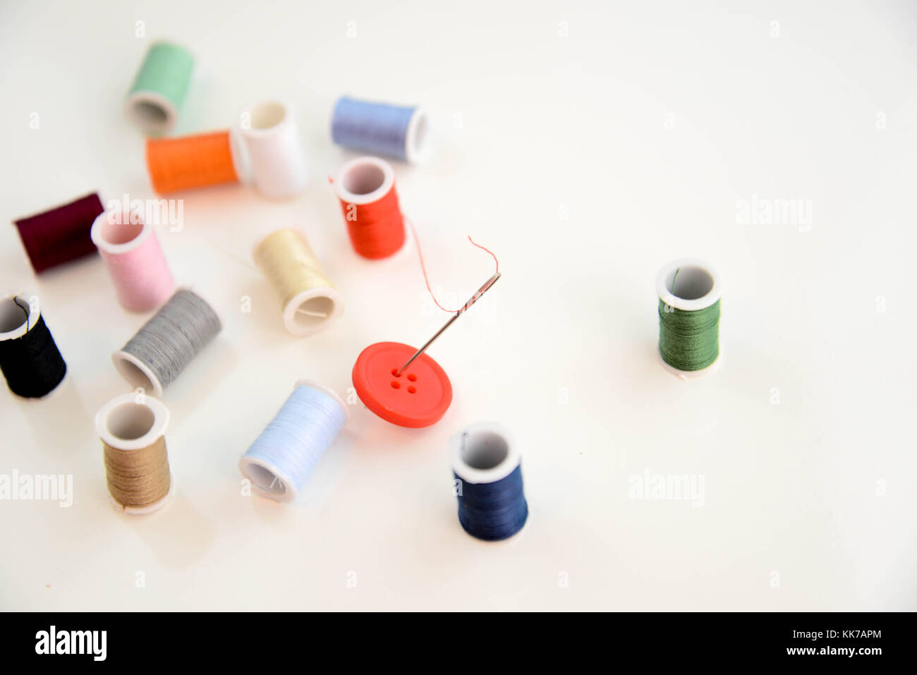 red thread through needle eye and red button with multi colored thread ...