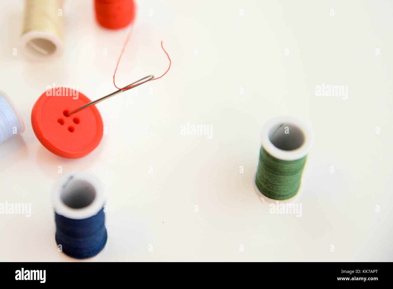 red thread through needle eye and red button with multi colored thread ...