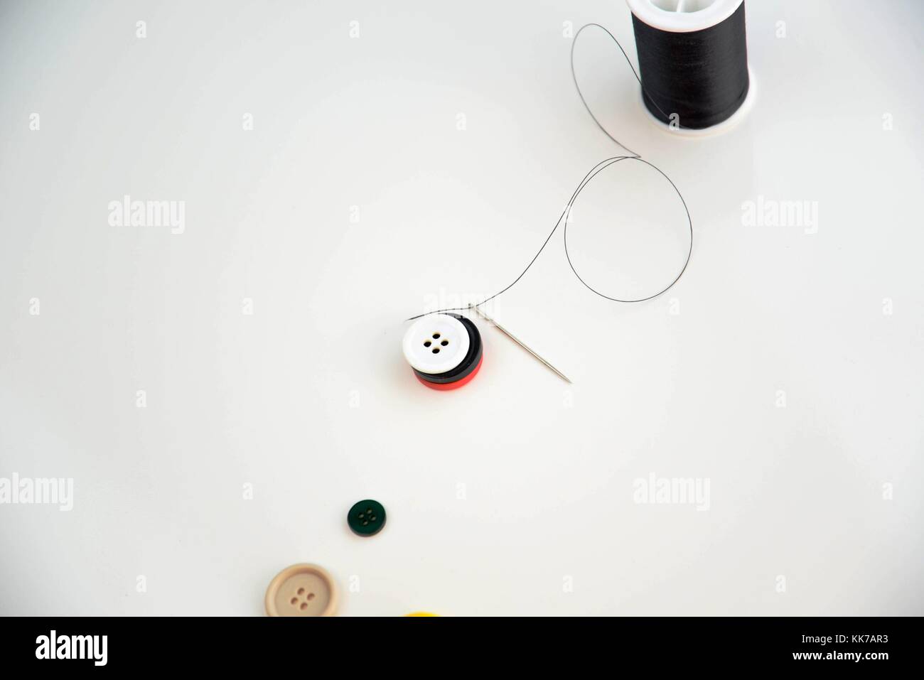 threaded needle, buttons, and black spool of thread Stock Photo - Alamy