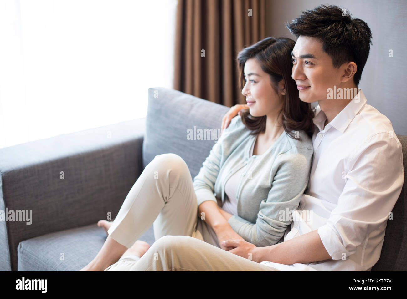 Happy young Chinese couple sitting on sofa at home Stock Photo - Alamy