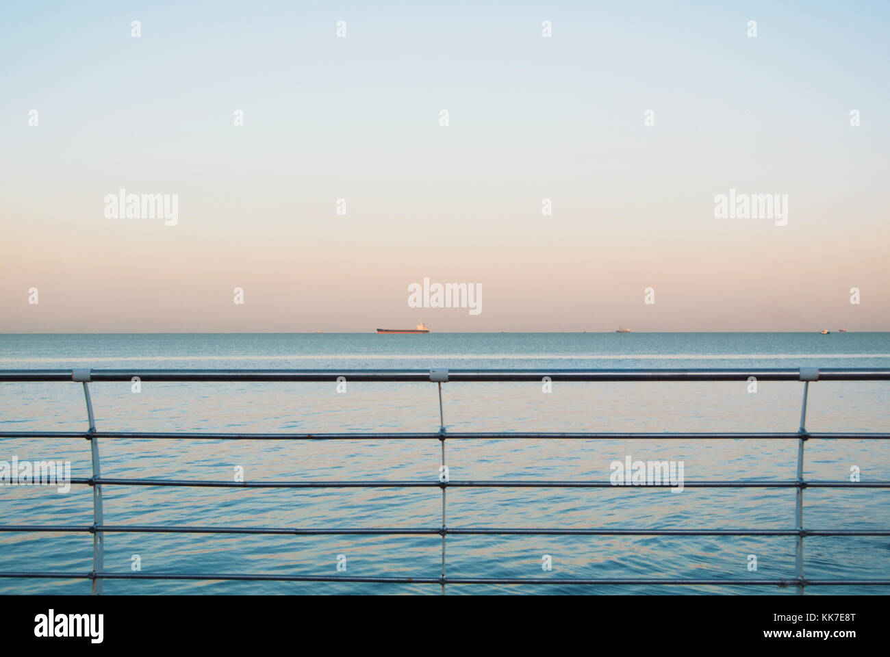 A view to a sea with a cargo ship at the background and a metal fence ...