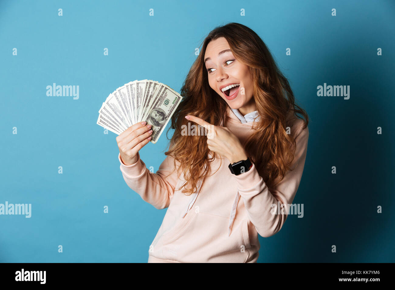 Portrait of a smiling attractive girl pointing finger at bunch of money ...