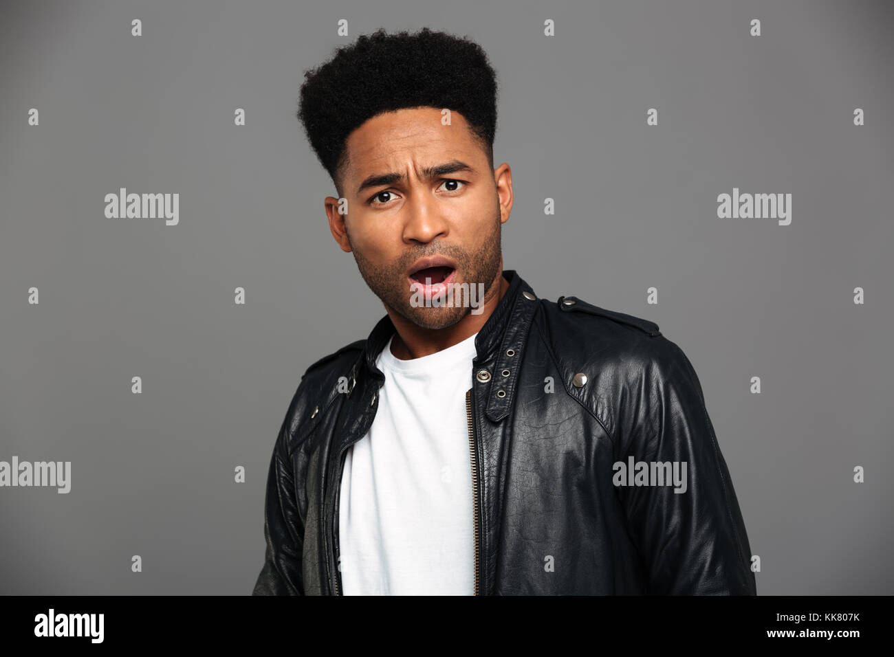 Portrait of a surprised shocked african man in leather jacket looking at camera isolated over ...