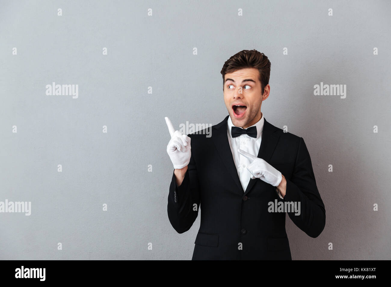 Photo of shocked young waiter standing isolated over grey wall ...