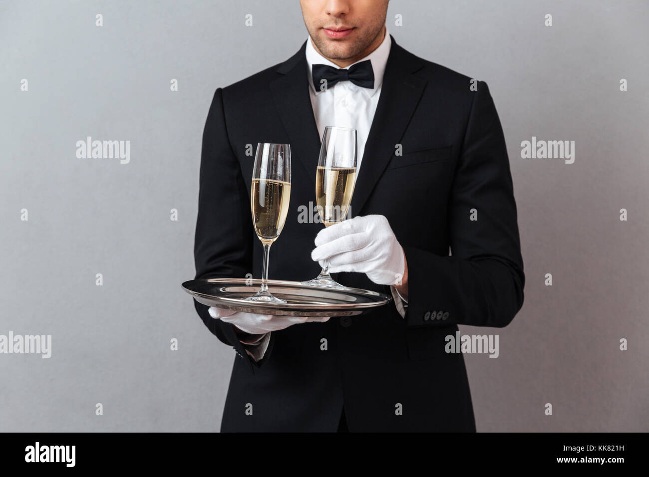 Cropped image of young waiter standing isolated over grey wall ...