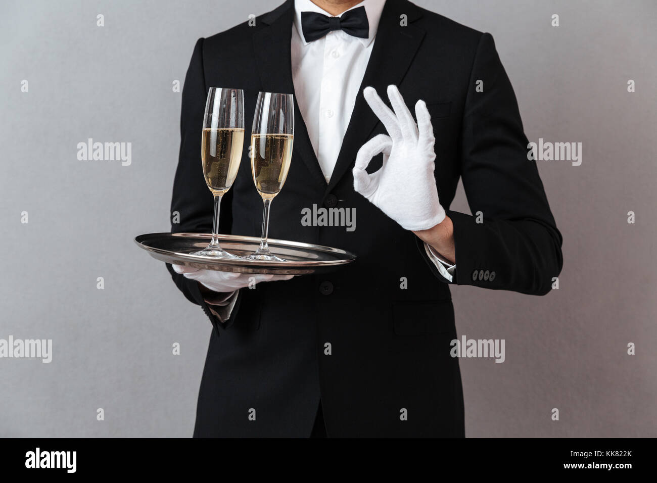 Cropped image of young waiter standing isolated over grey wall ...