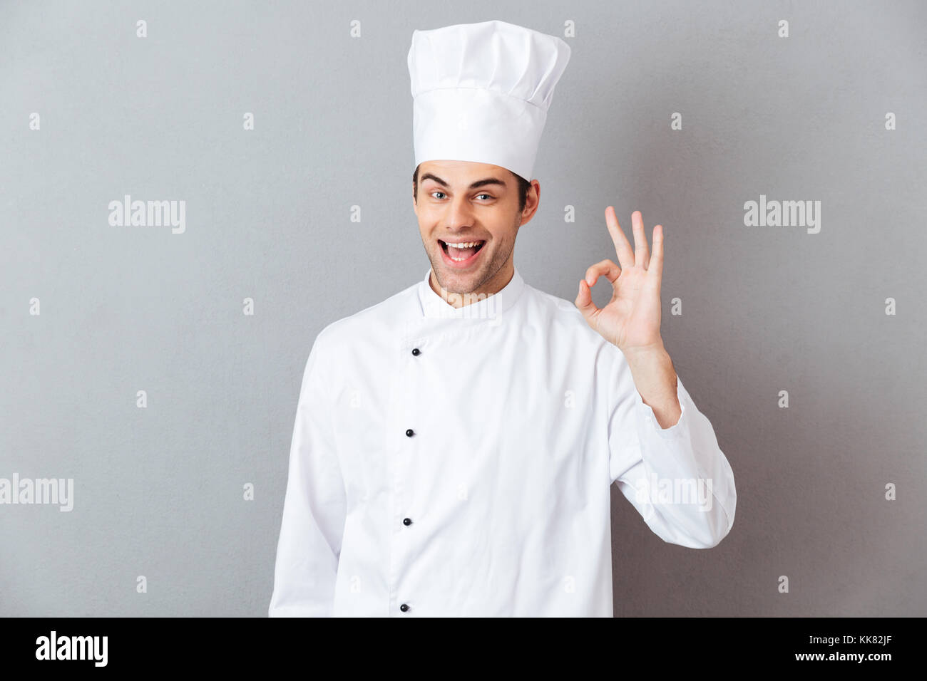 Image of cheerful young cook in uniform standing isolated over grey ...