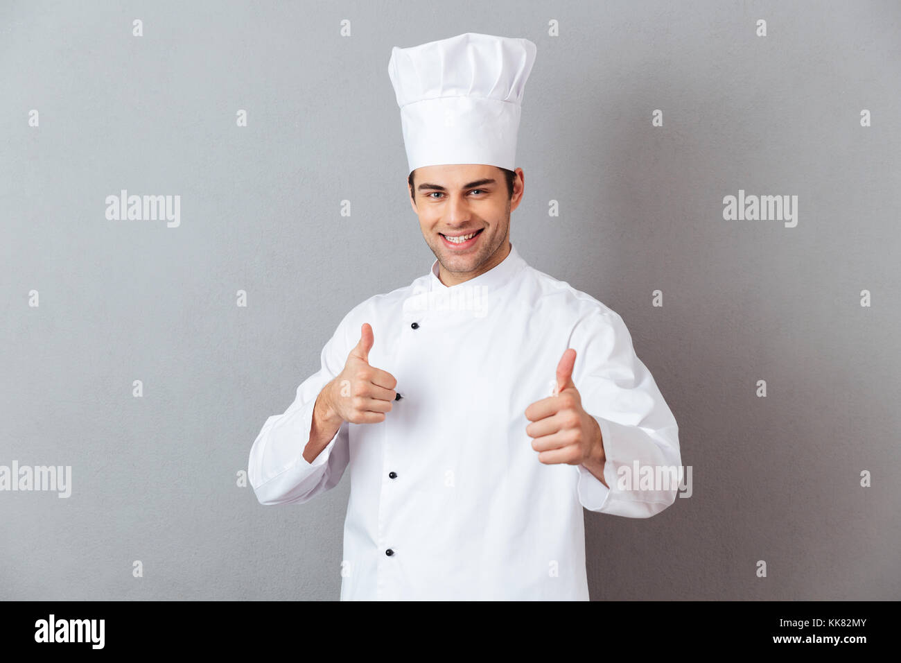 Photo of smiling emotional young cook in uniform standing isolated over ...
